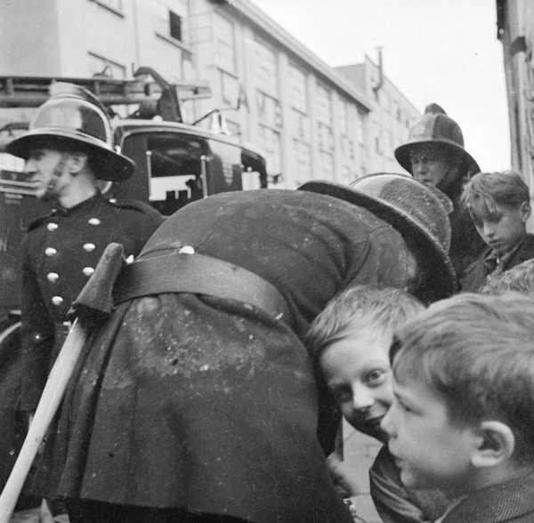 Photograph showing firefighters, a group of children watching them ...