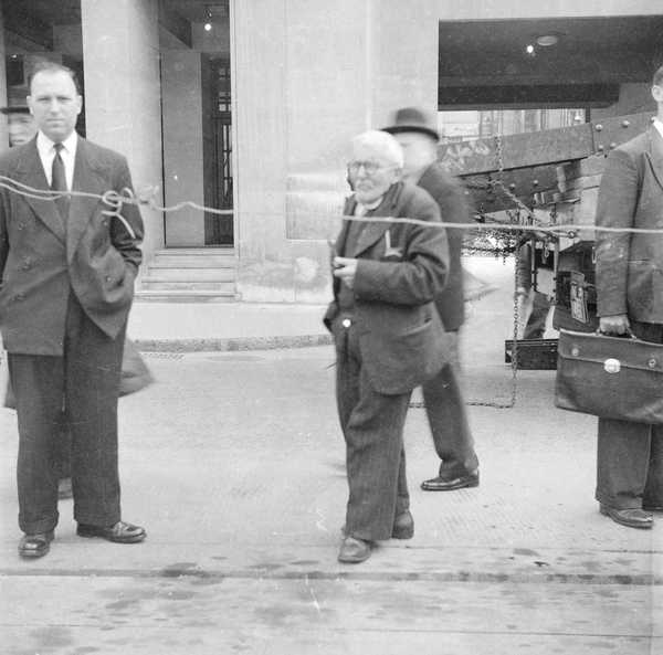 Photograph showing a group of men behind a rope, building under ...