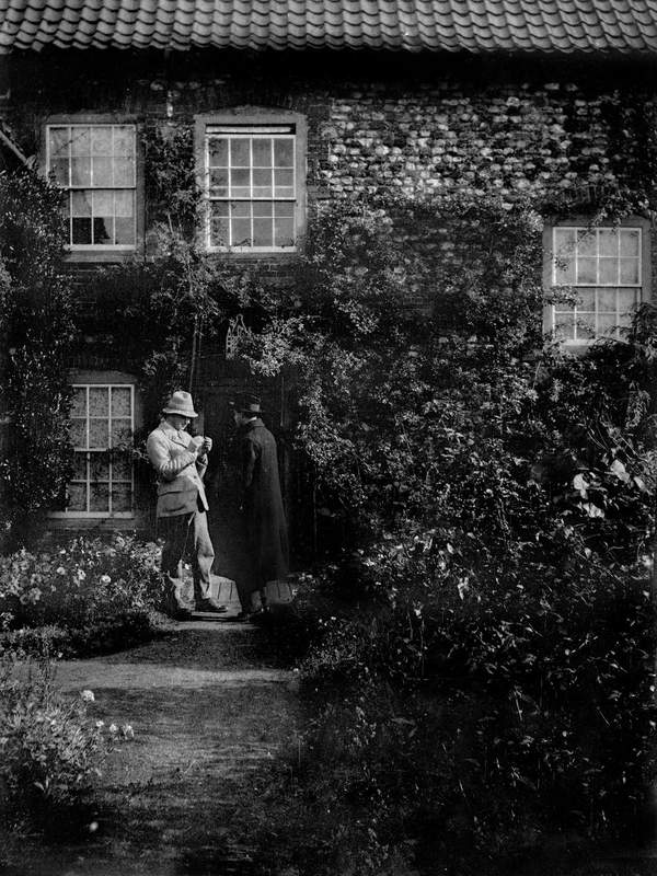 Black and white negative of two unidentified figures in front of an ivy ...