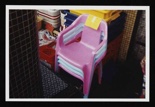 Colour photograph of blue and pink plastic chairs stacked up outside a ...