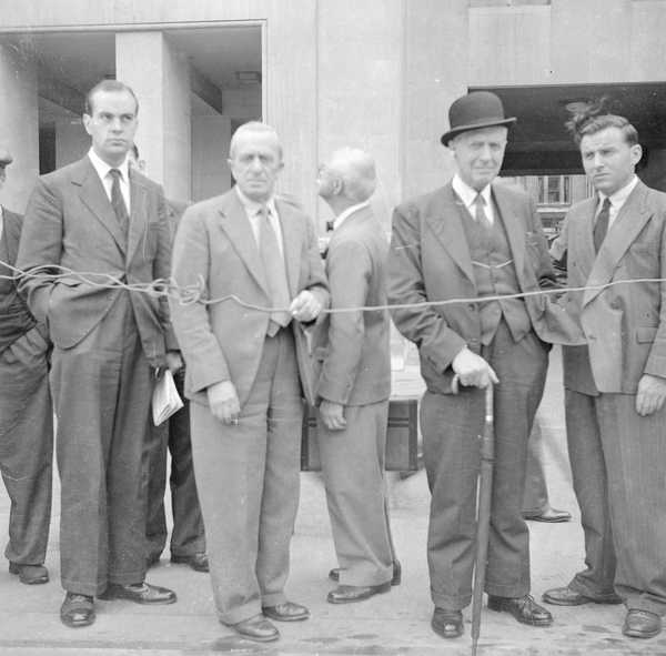 Photograph showing a group of men behind a rope, a building under ...