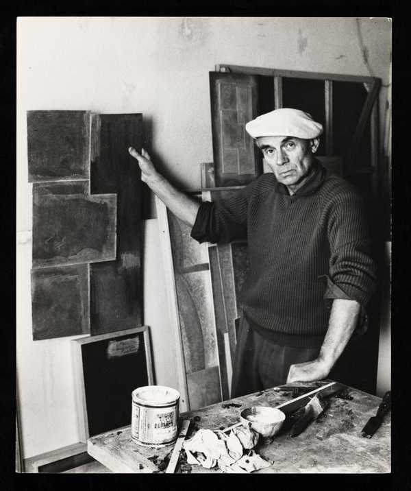 Photograph of Ben Nicholson with his hand on one of his art works in ...